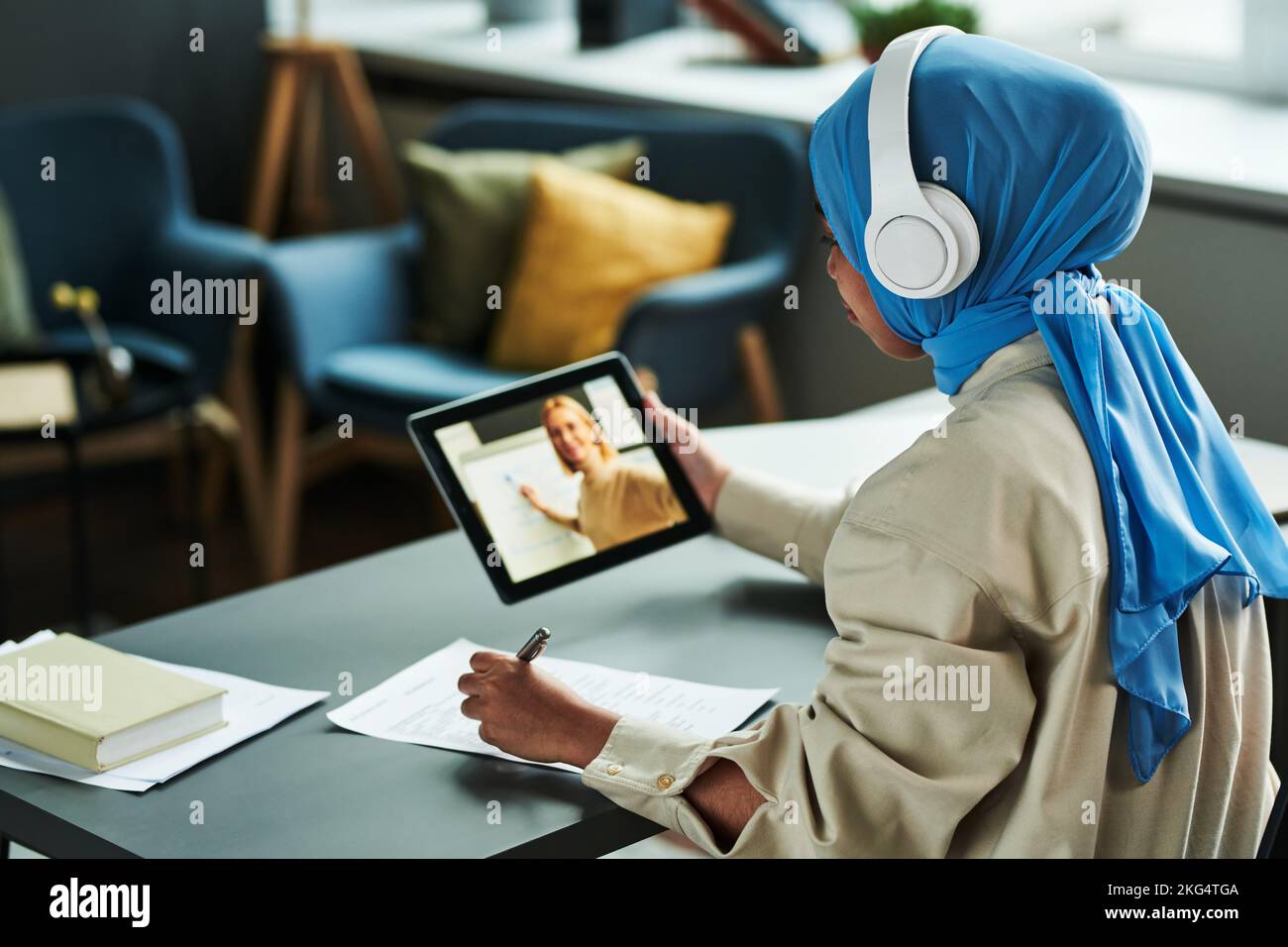 Young Muslim woman in blue hijab and white headphones listening to ... Young Muslim woman in blue hijab and white headphones listening to ...