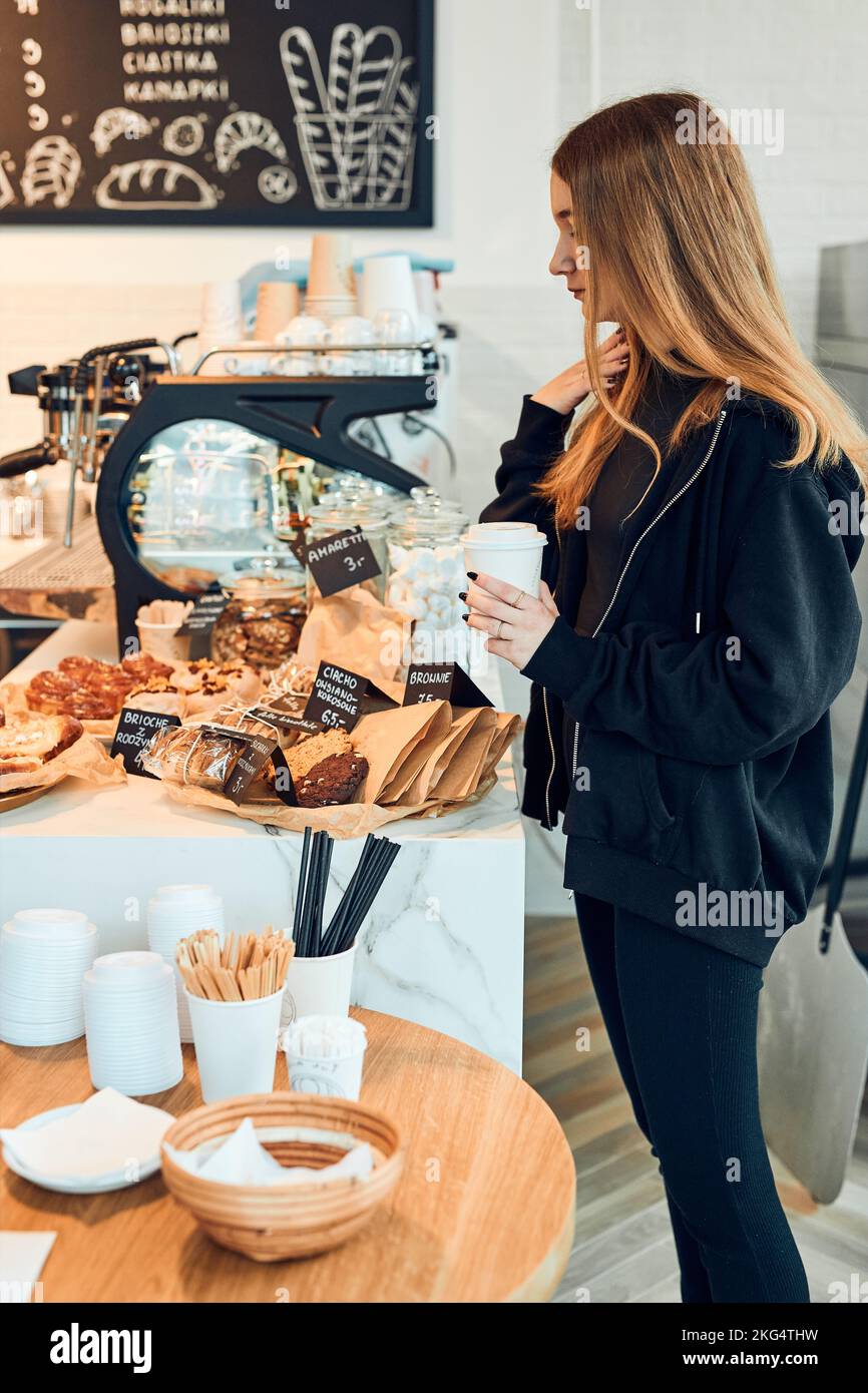 Woman holding cup with coffee looking at pastry, buns, cakes and ...
