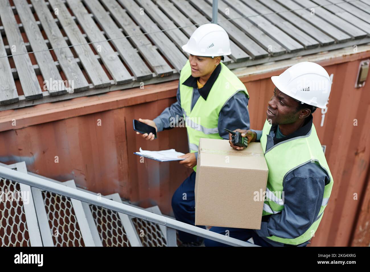 High angle portrait of two workers carrying boxes up stairs at shipping ...