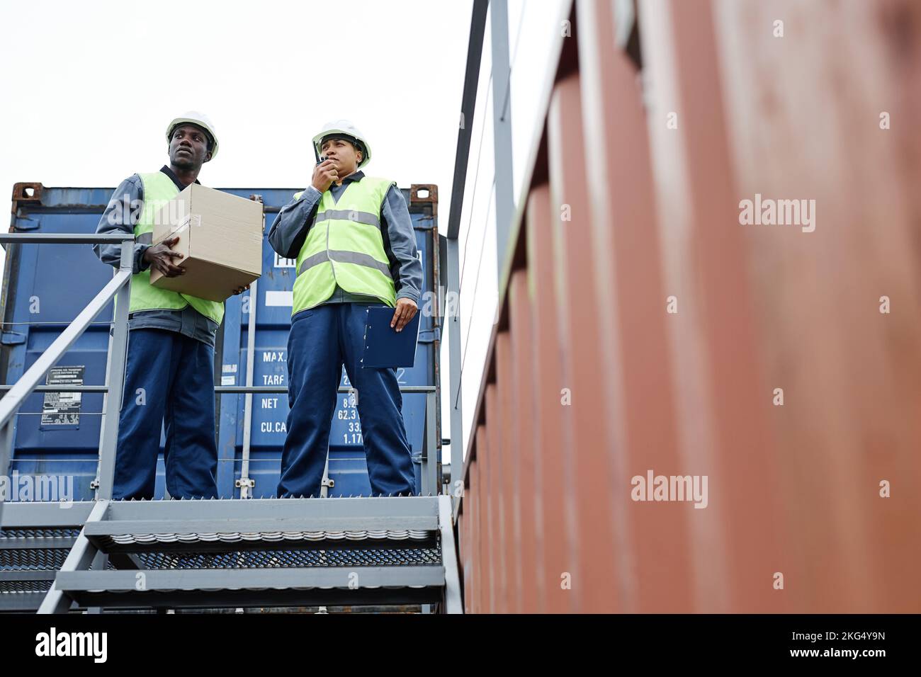Full length portrait of two workers standing on container at shipping ...