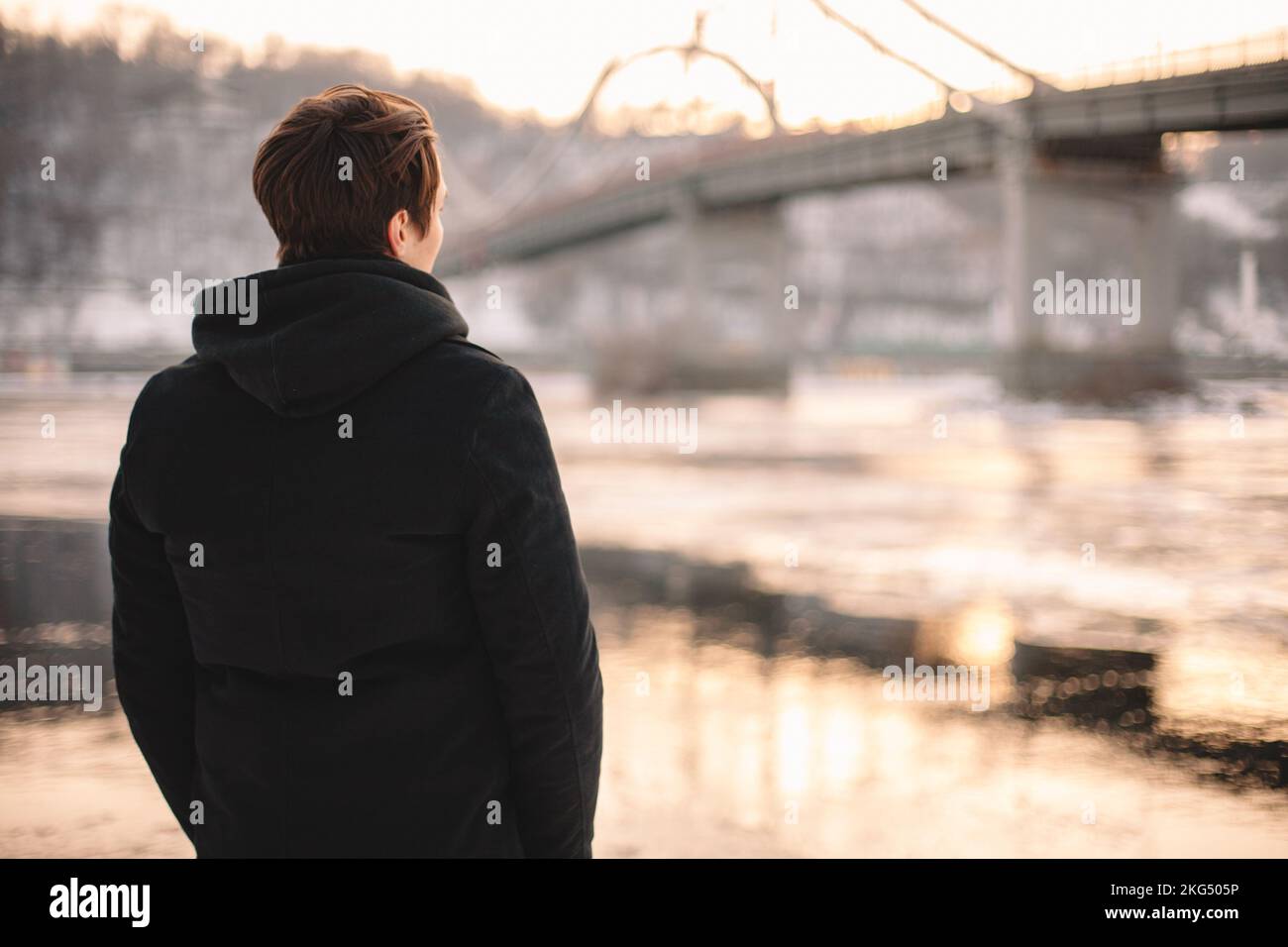 Back view of thoughtful young man looking at river while standing ...