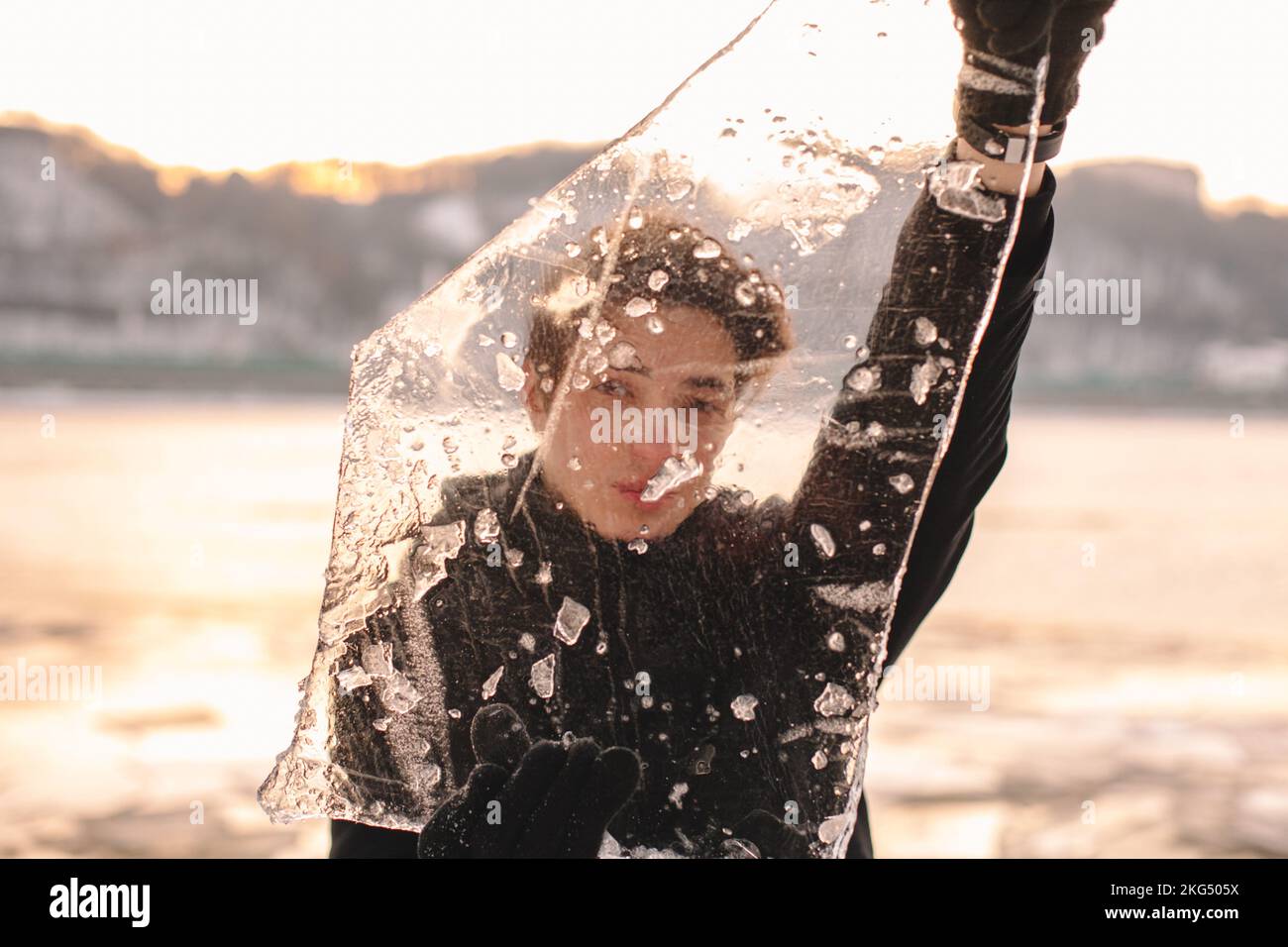 Teenage boy looking through chunk of ice while holding it standing ...
