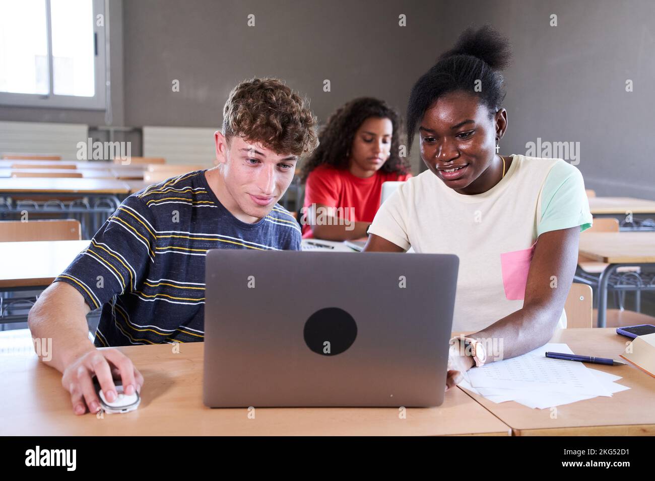 Young multiracial students using laptop while sitting on desk in the ...