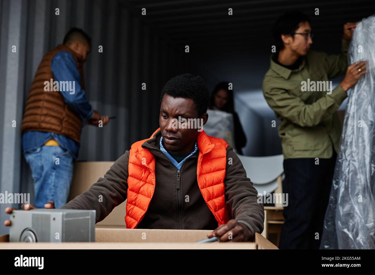 Portrait of young black man at outdoor auction opening cardboard boxes ...