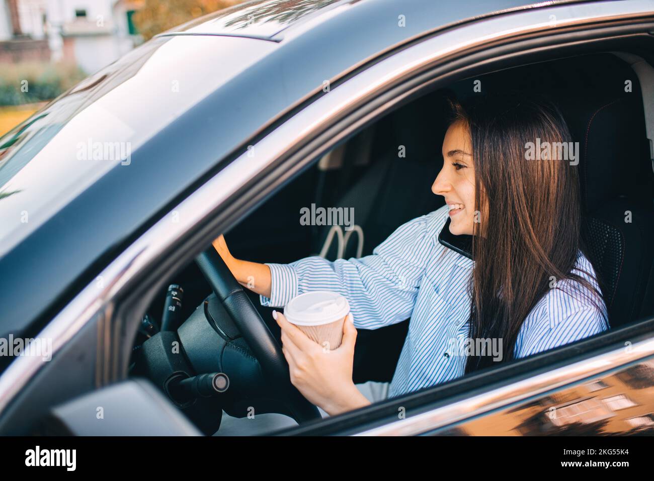 Side view of woman driving car with coffee to go in hand. Young woman ...