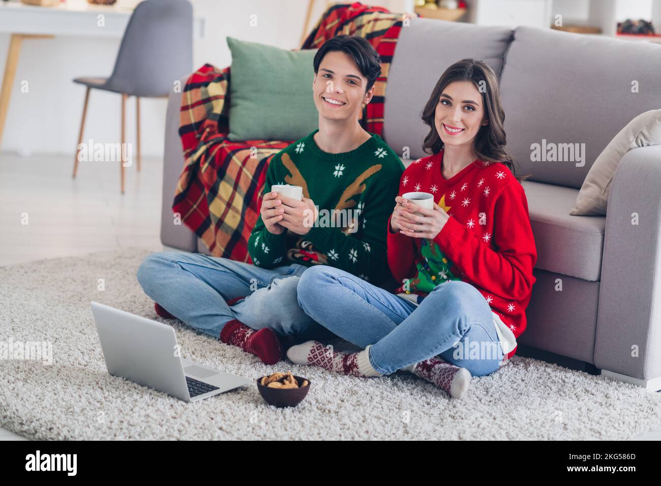Photo of two young smiling cute man with wife chill near couch hold mug ...