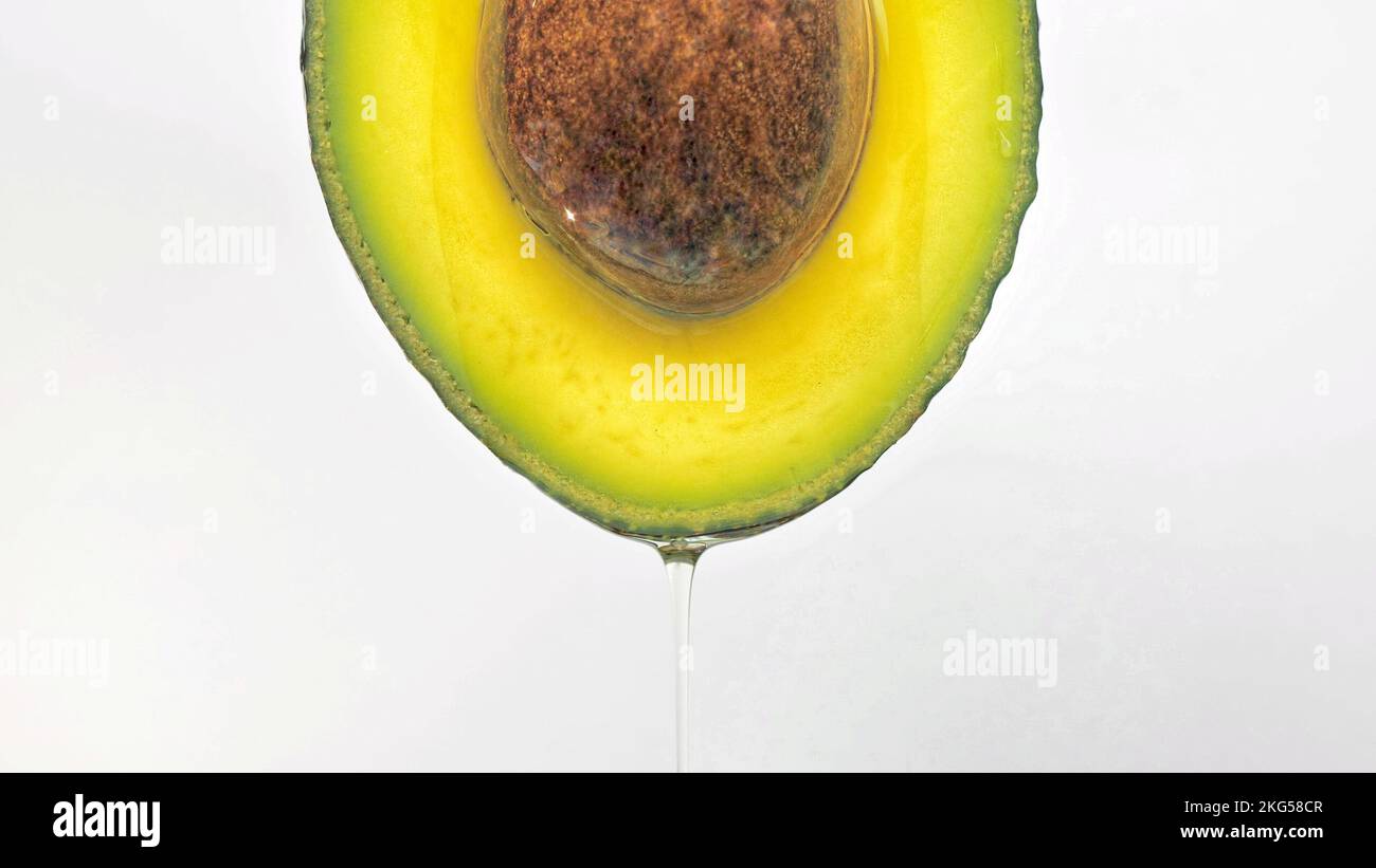 Avocado oil concept on white background. Avocado oil drips off half an ...