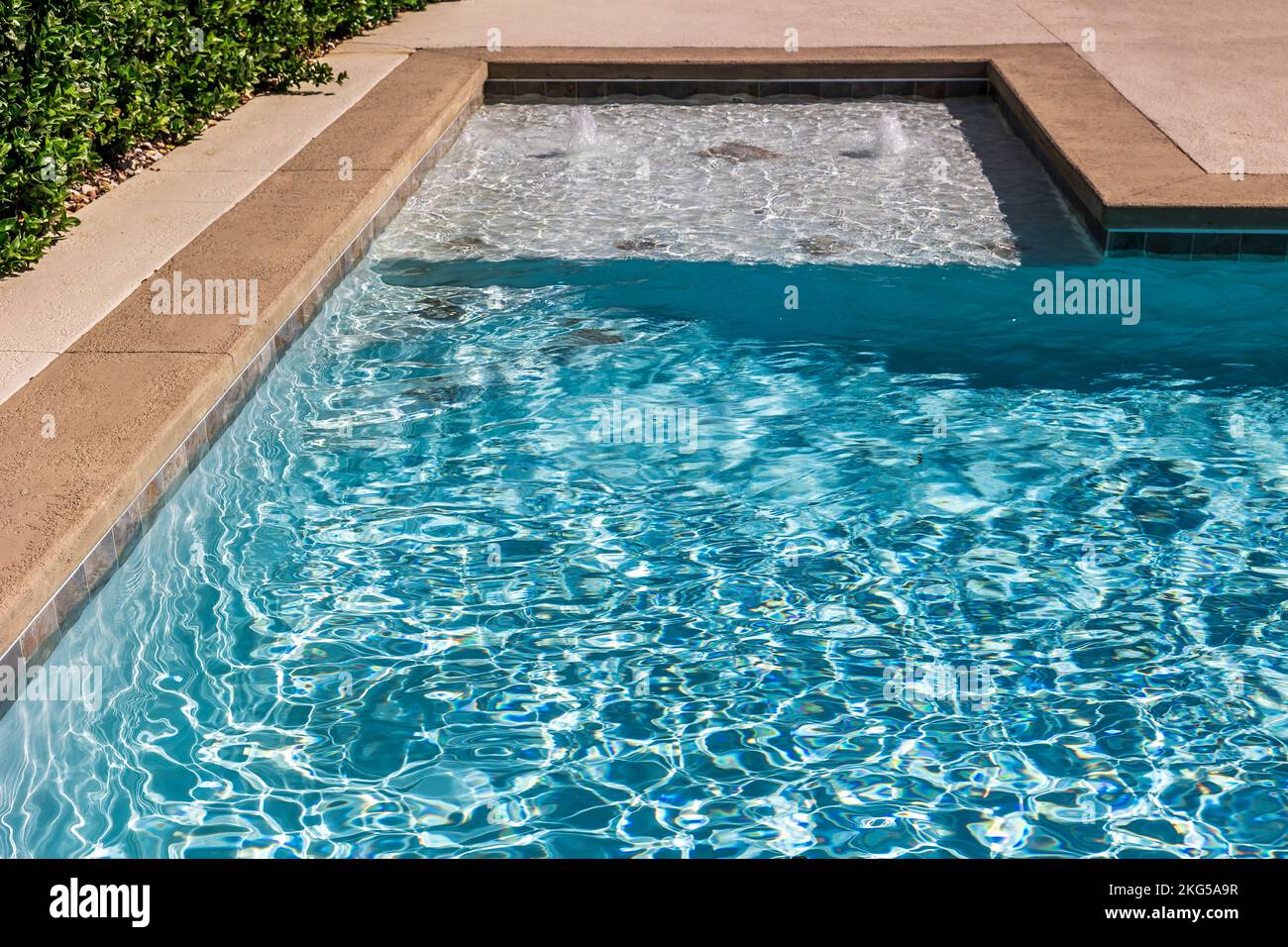 A rectangular new swimming pool with tan concrete edges in the fenced ...