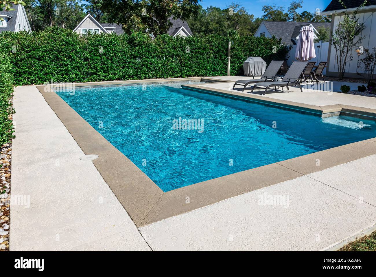 A rectangular new swimming pool with tan concrete edges in the fenced ...
