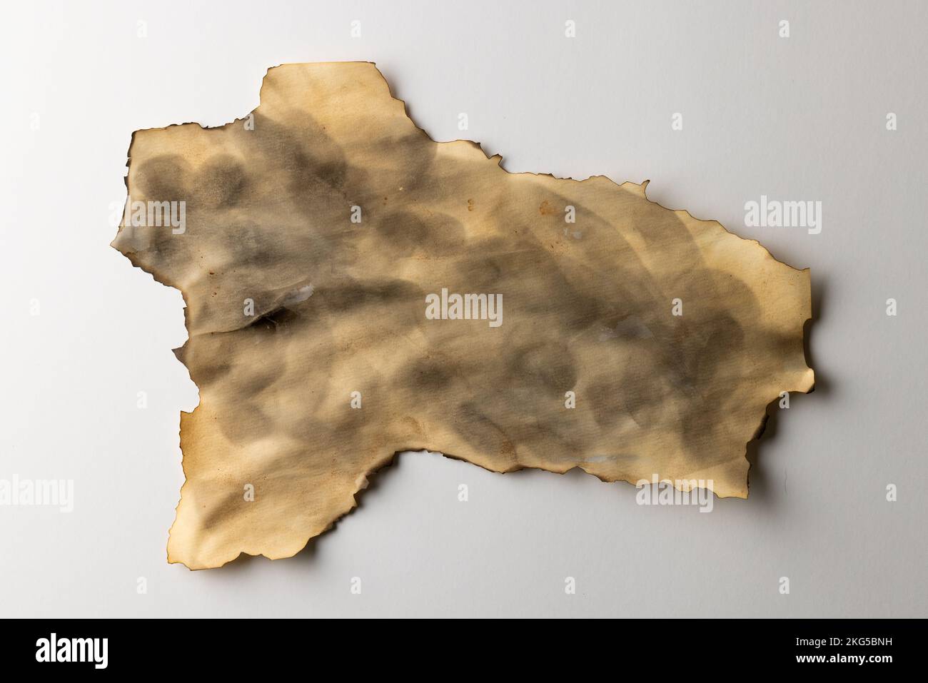Burned and stained piece of paper with copy space on white background ...