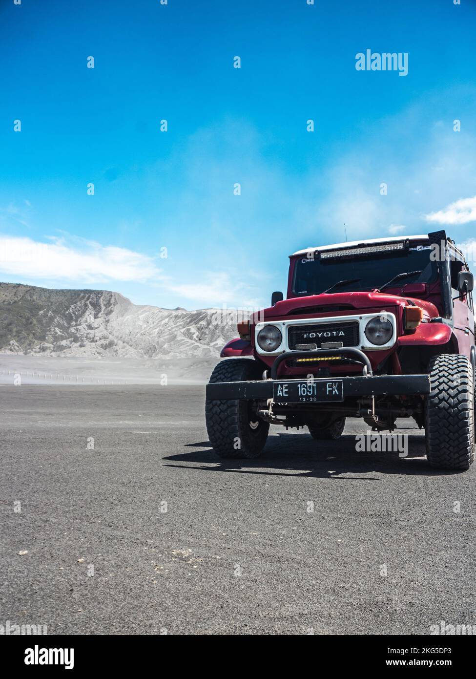 A vertical closeup shot of a red Jeep land cruiser on a sandy surface ...