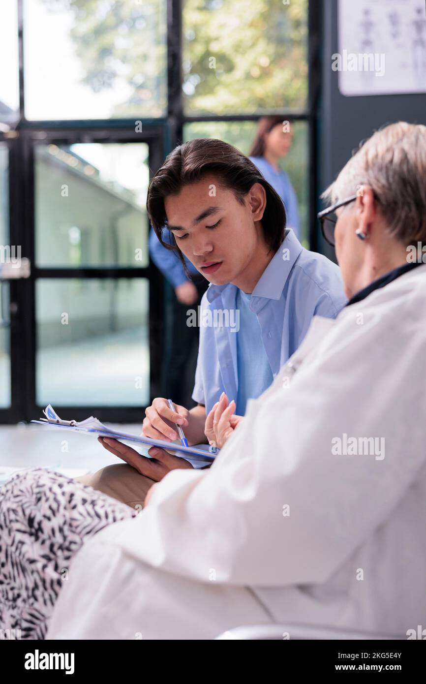 Young asian patient signing medical document while elderly doctor ...