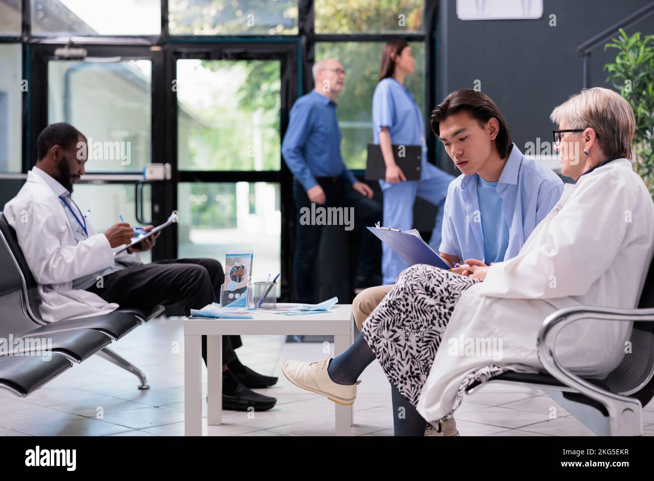 Elderly doctor standing beside asian patient helping to fill medical ...
