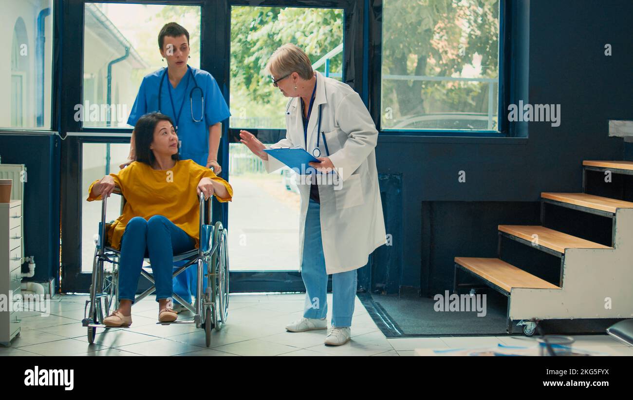 Medical assistant helping patient in wheelchair with impairment ...