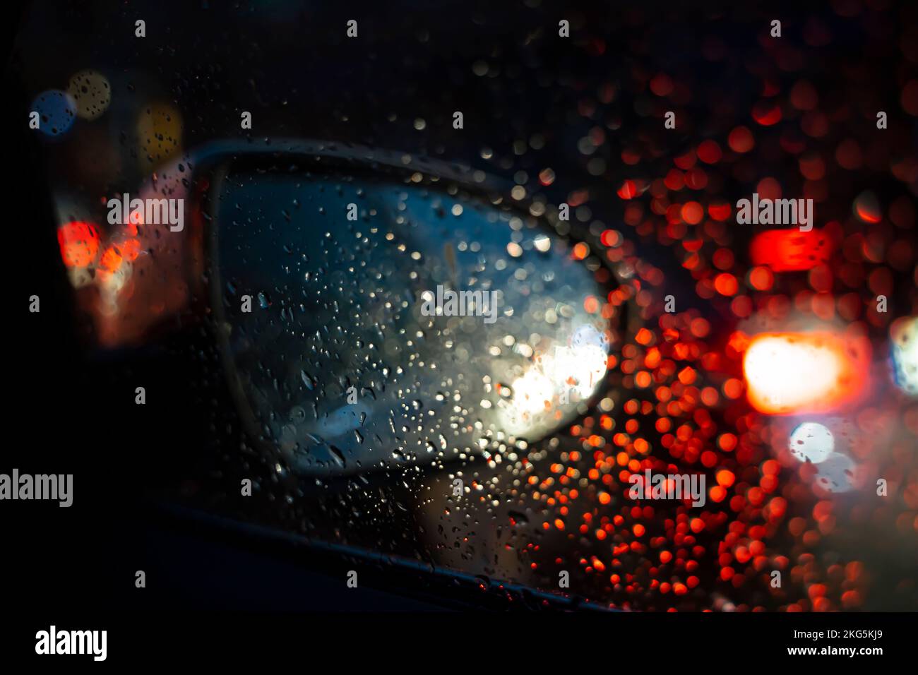Out of focus car side view mirror with rain drops seen through wet ...