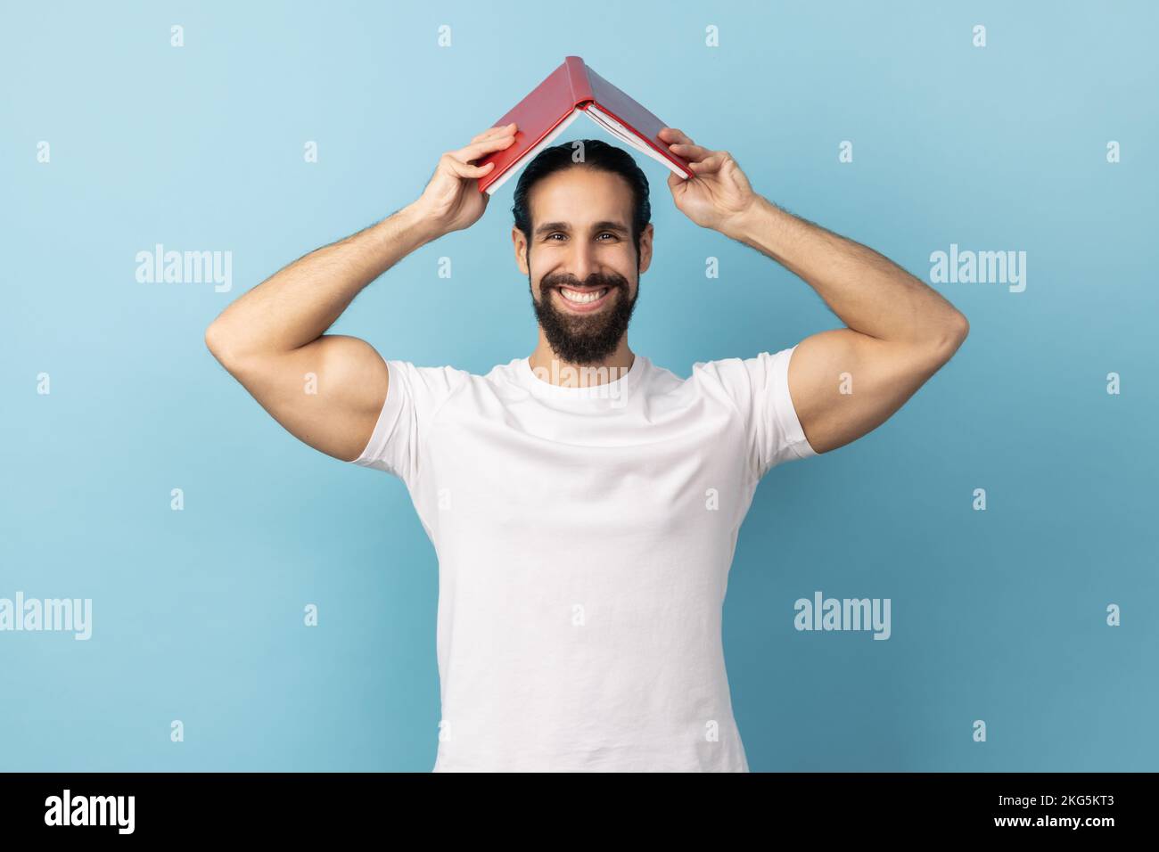 Portrait of delighted man with beard wearing white T-shirt making roof ...