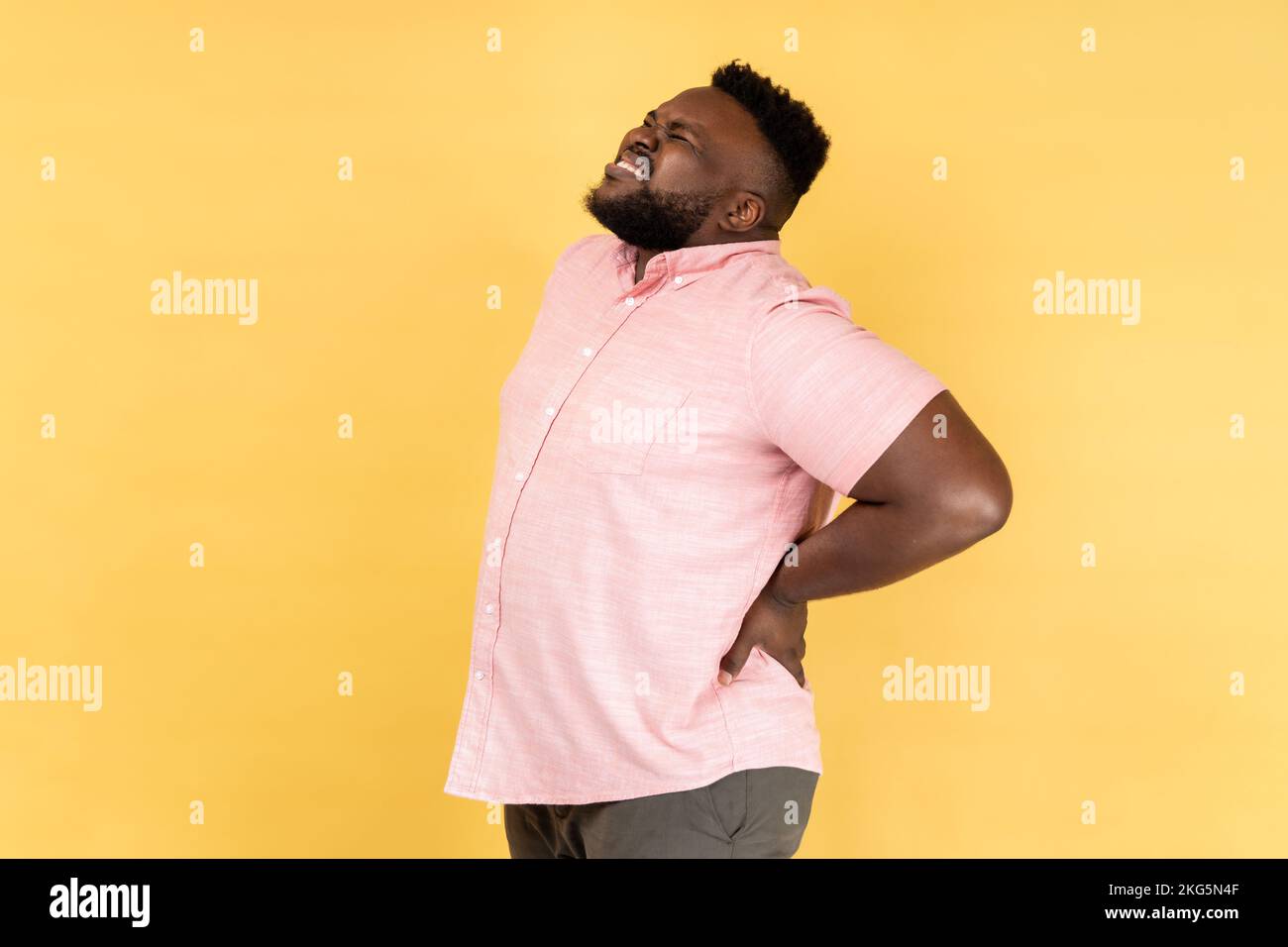 Back, kidney or spine pain. Portrait of man wearing pink shirt standing ...