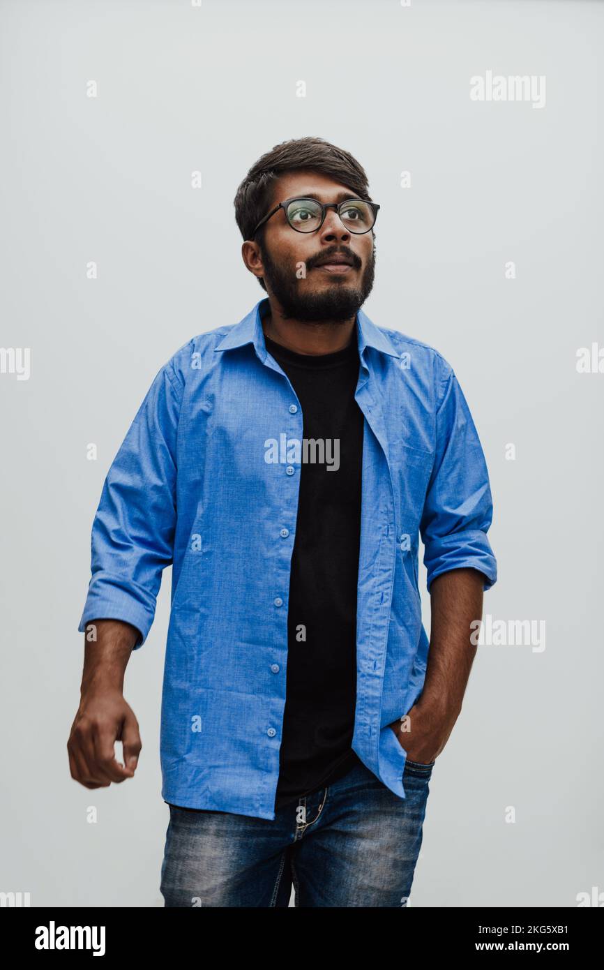 Indian smiling young man with blue shirt and glasses posing on gray ...