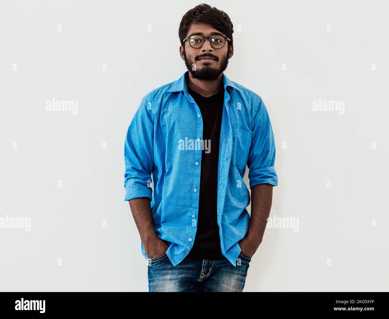 Indian smiling young man with blue shirt and glasses posing on gray ...