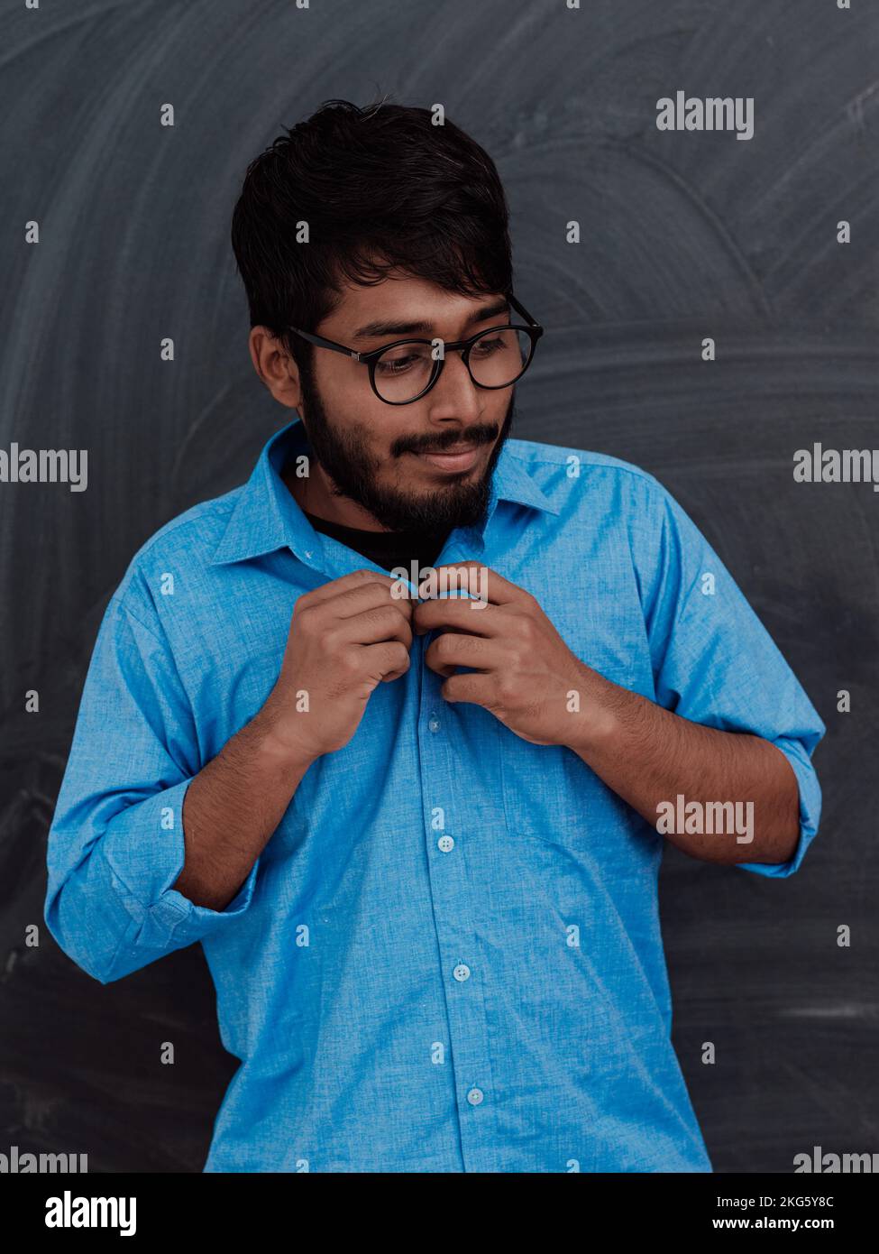 Indian young student wearing glasses puts on a blue shirt while ...