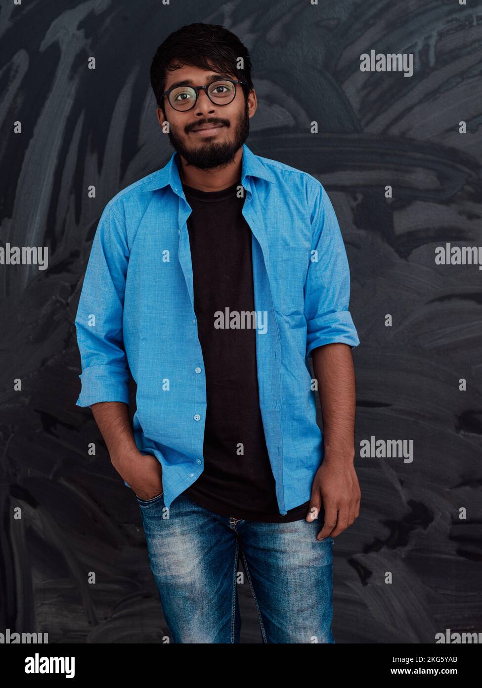 Indian smiling young student in blue shirt and glasses posing on school ...
