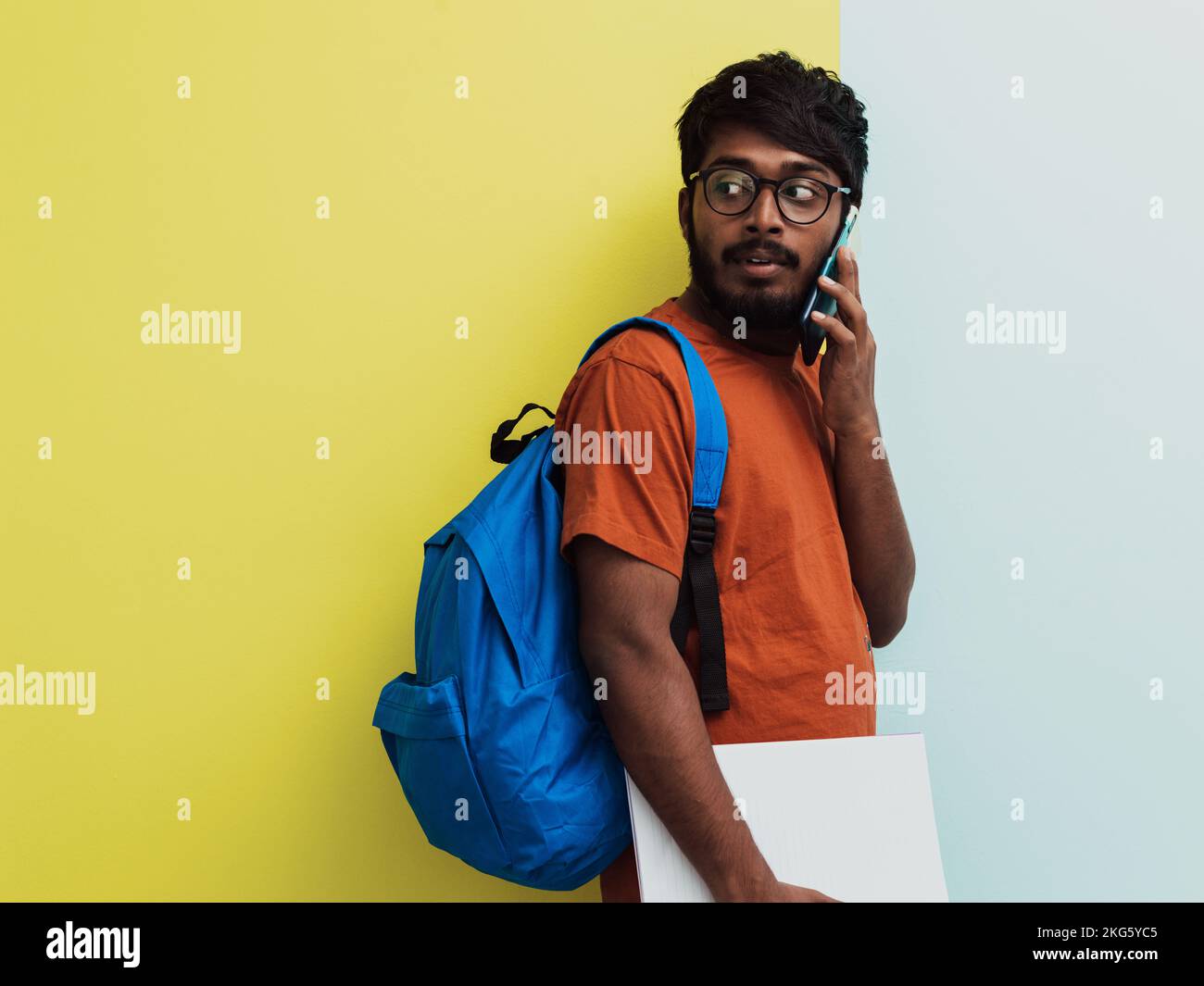 Indian student with blue backpack, glasses and notebook posing on gray ...