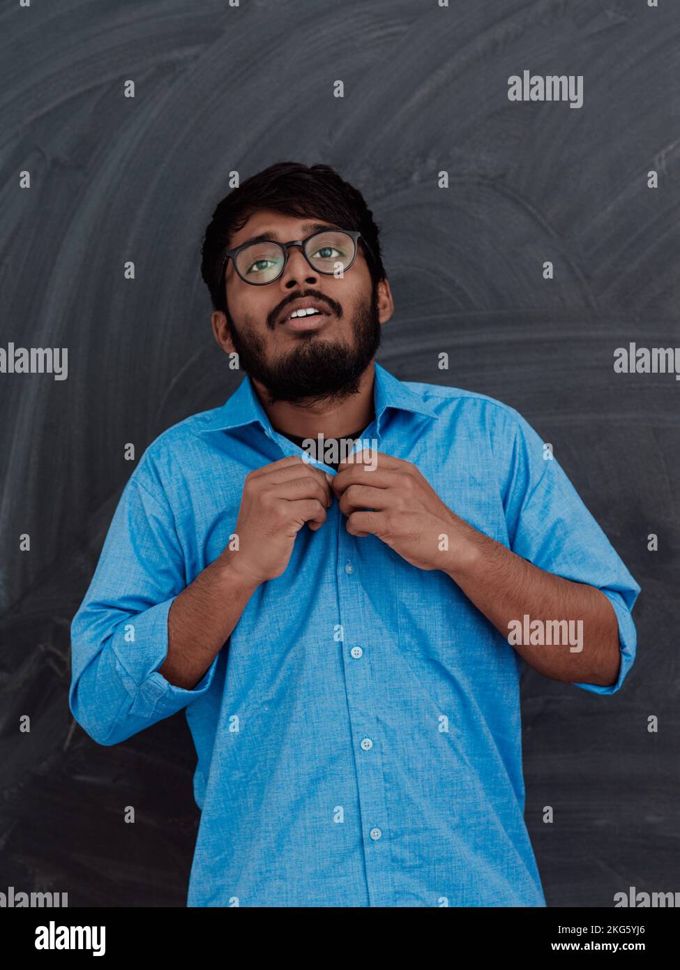 Indian young student wearing glasses puts on a blue shirt while ...