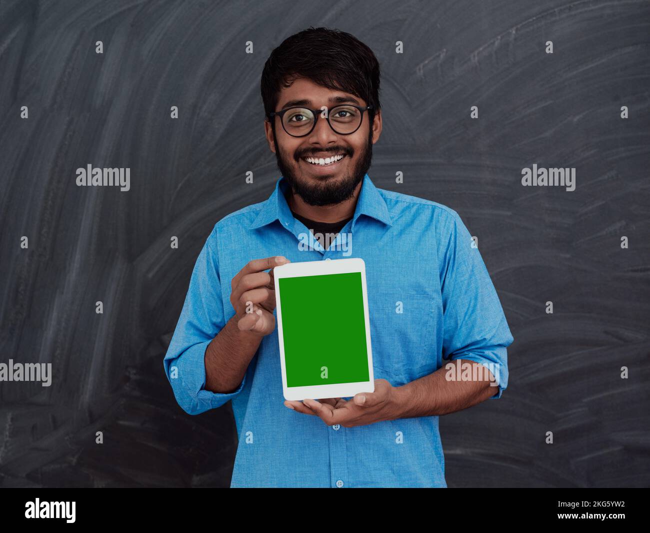 Indian smiling young student in blue shirt and glasses using tablet ...