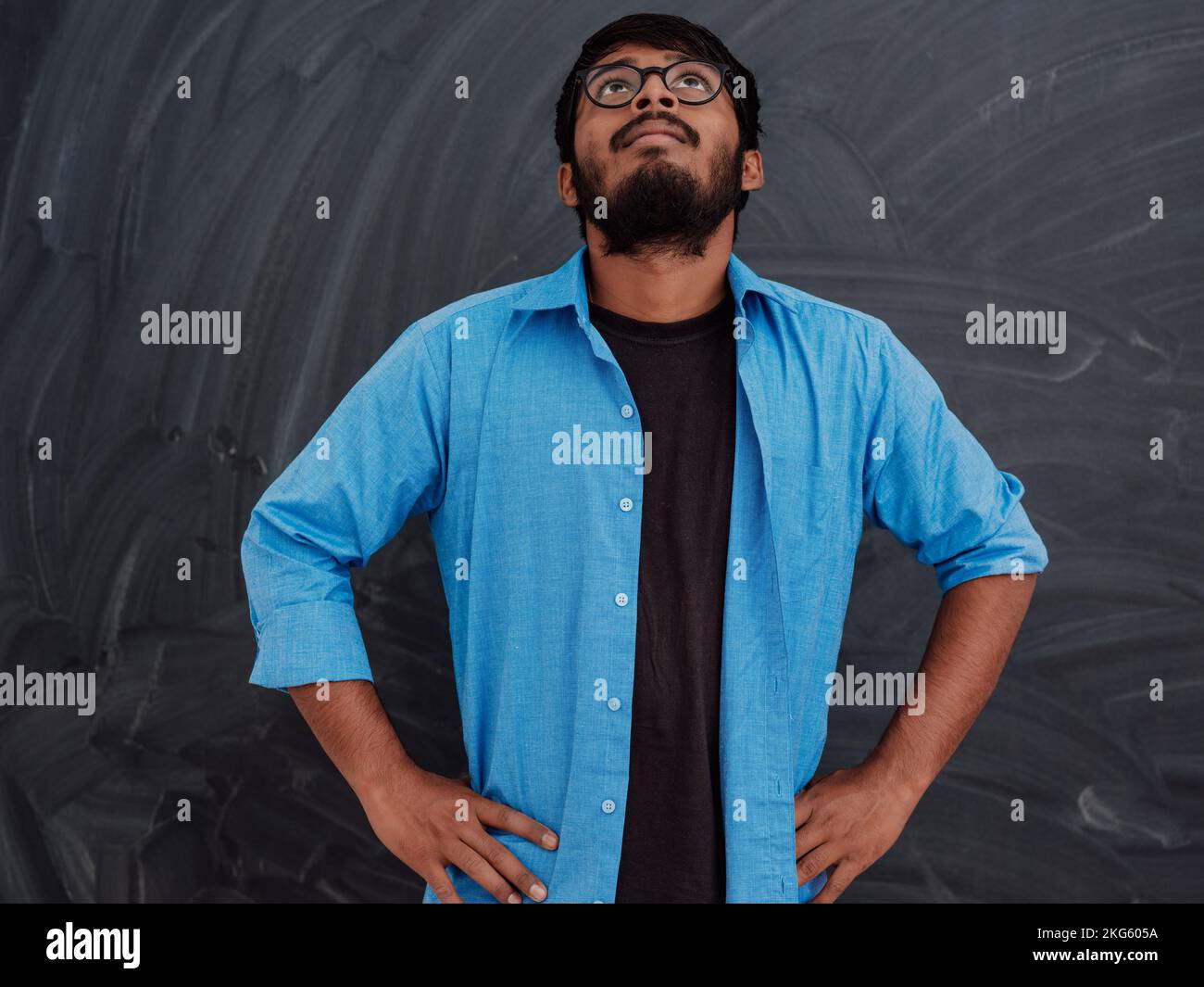 Indian smiling young student in blue shirt and glasses posing on school ...