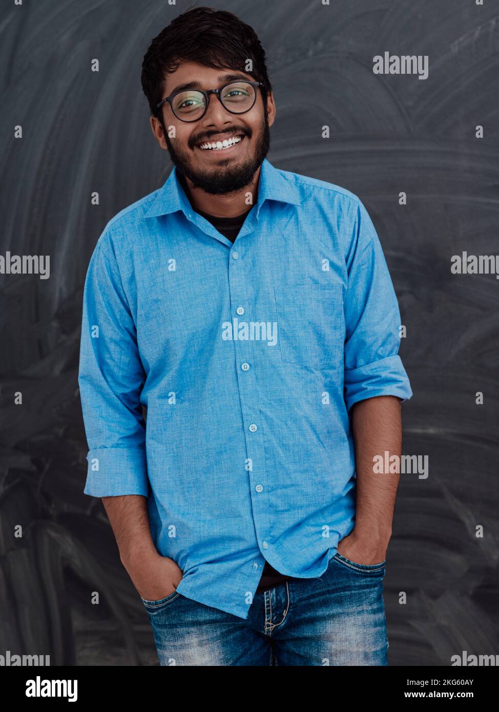 Indian smiling young student in blue shirt and glasses posing on school ...