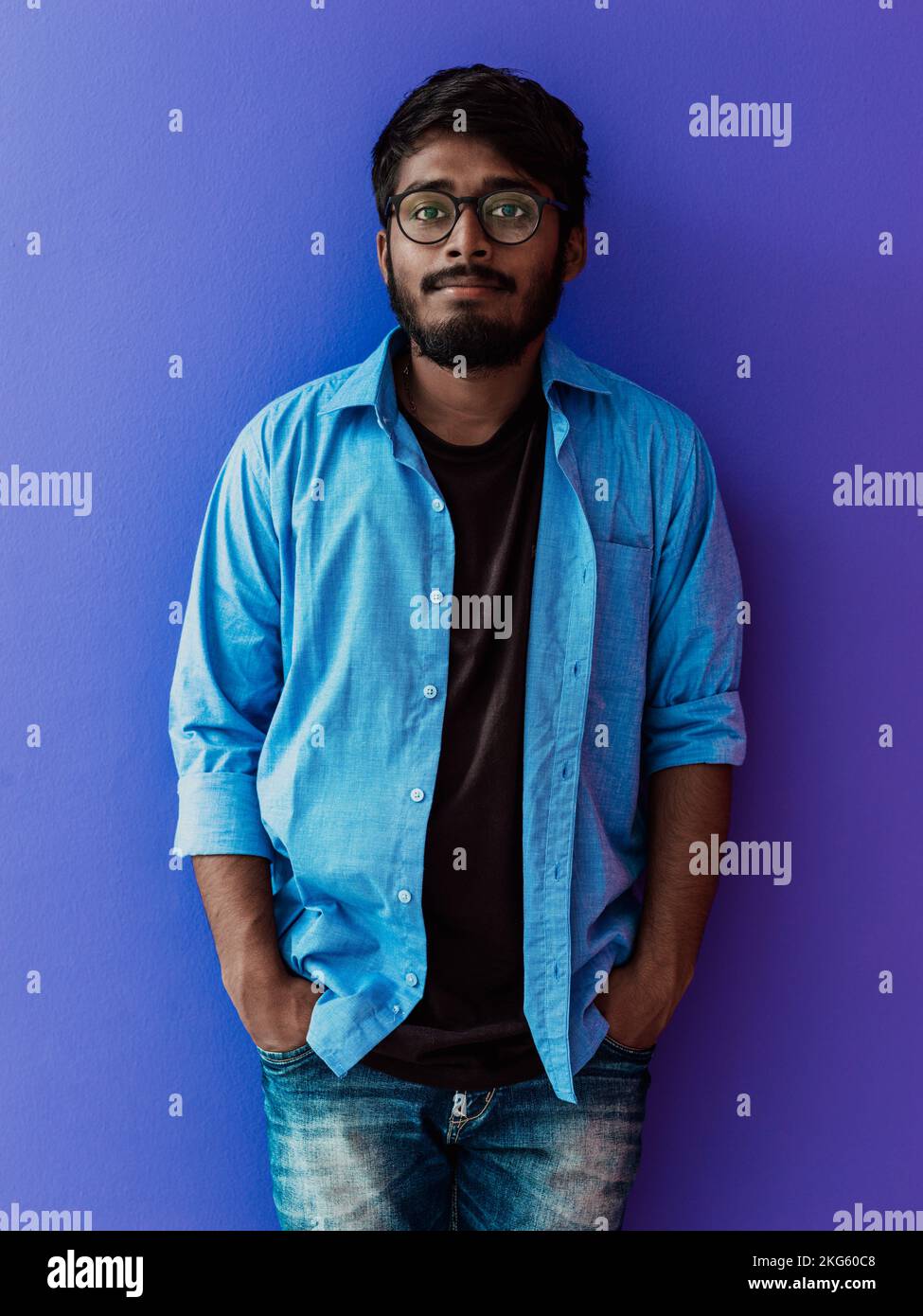 Indian smiling young man with blue shirt and glasses posing on purple ...