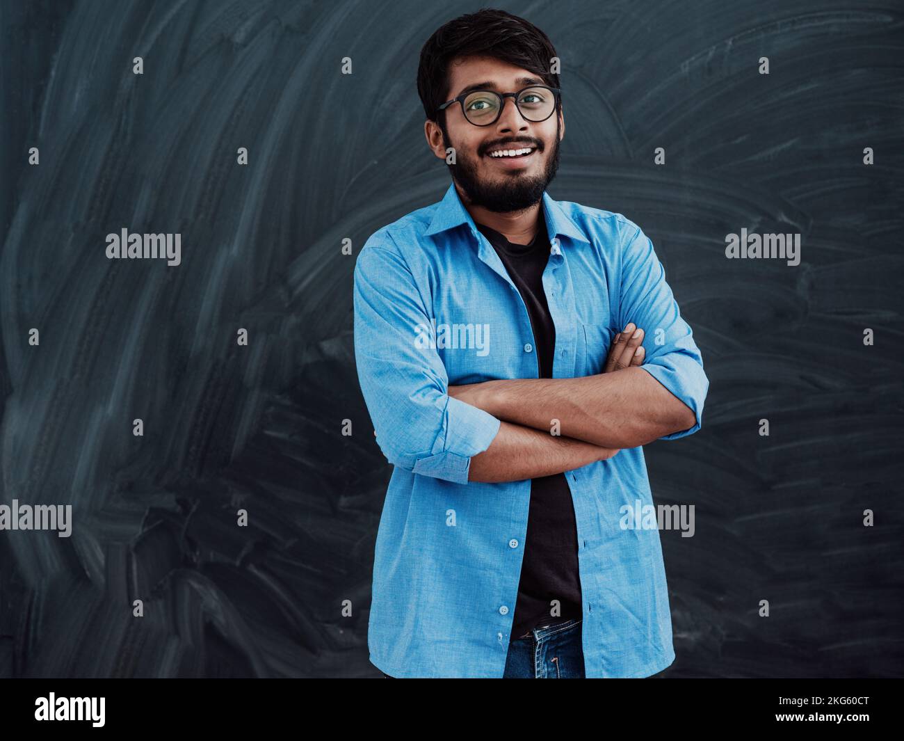 A young Indian student in a blue shirt with glasses posing with his ...