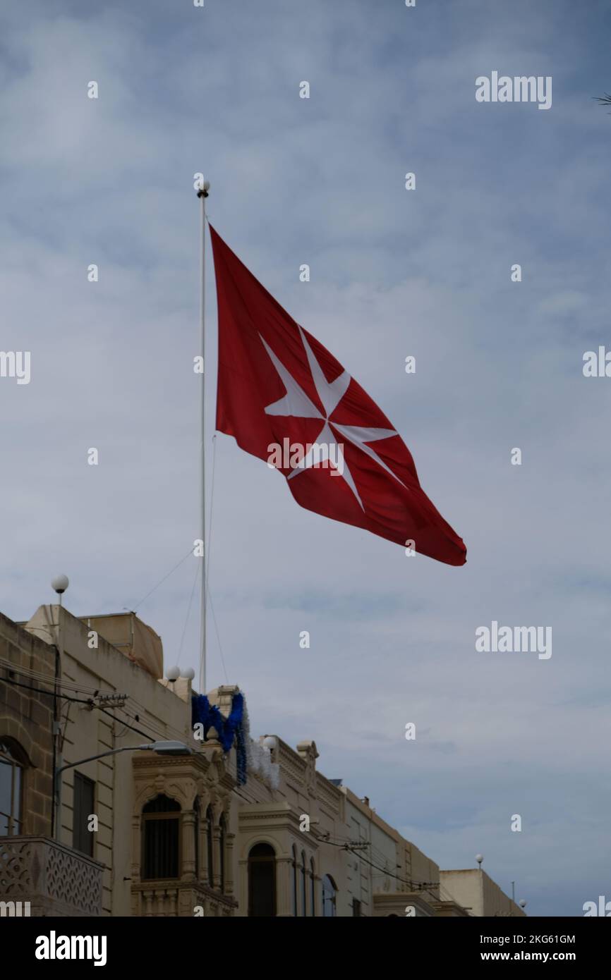 A vertical shot of the large Maltese flag waving over a government ...