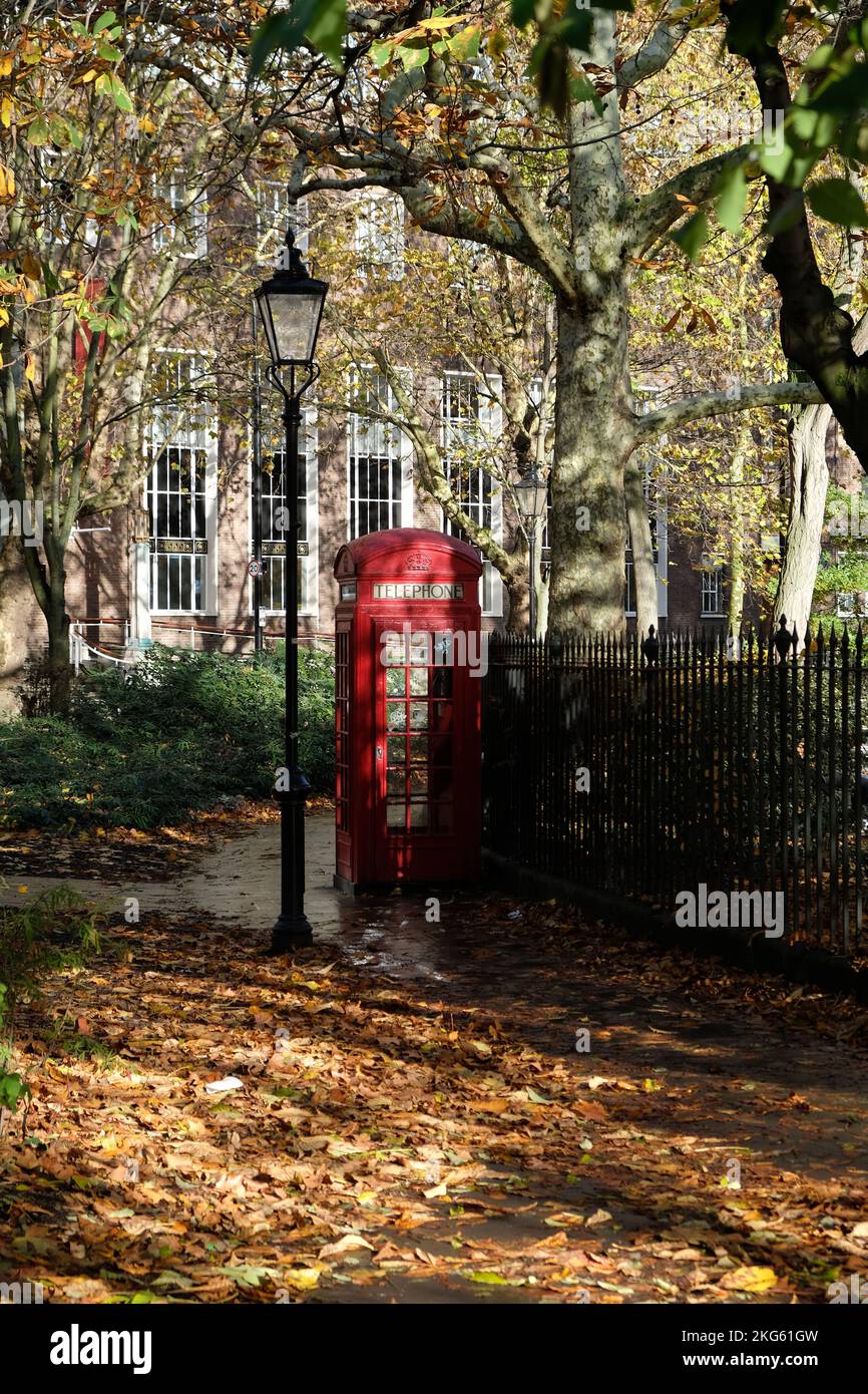 A vertical shot of the red phone booth in a park in London on ana ...