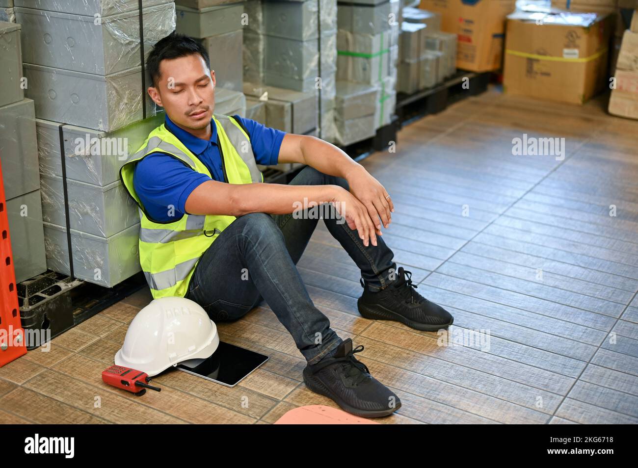 Tired and frustrated millennial Asian male warehouse worker sits on the ...