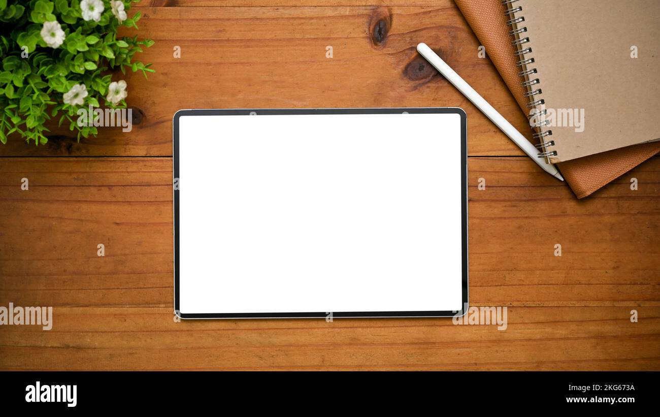 Digital tablet white screen mockup is on a wooden tabletop background with stylus pen, notebook ...
