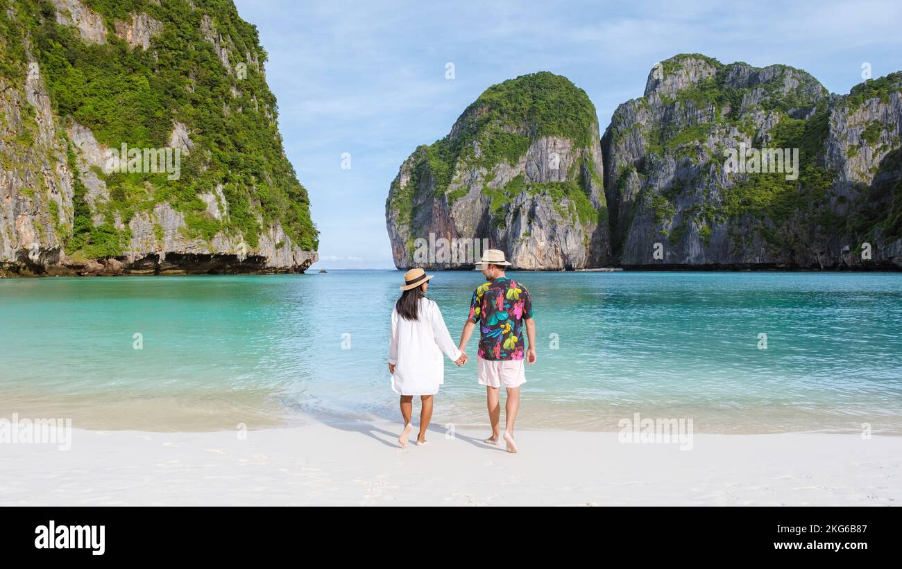 Thai women and caucasian men with a hat walk on the beach of Maya Bay ...