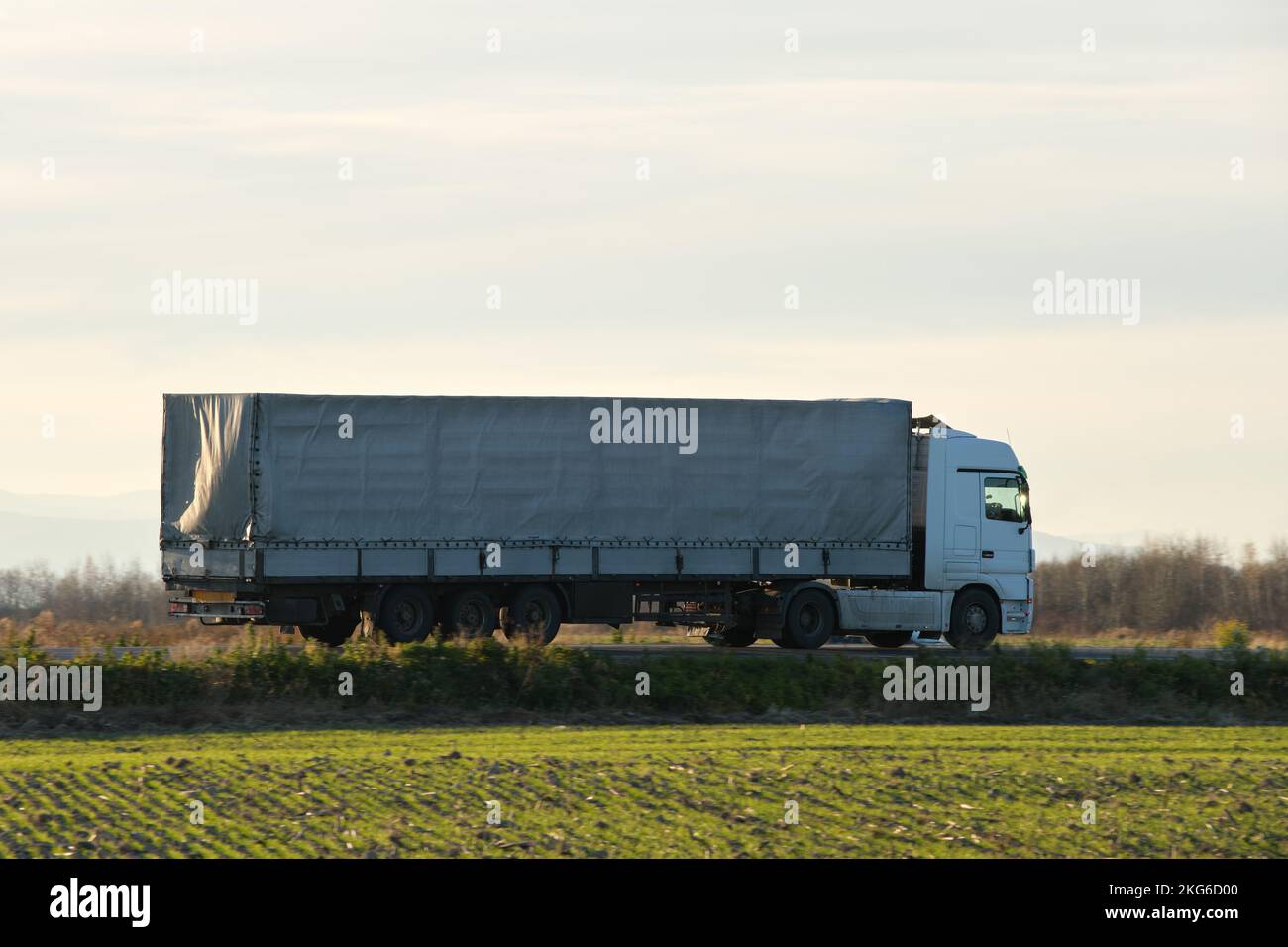 Semi-truck with cargo trailer driving on highway hauling goods in evening. Delivery ...