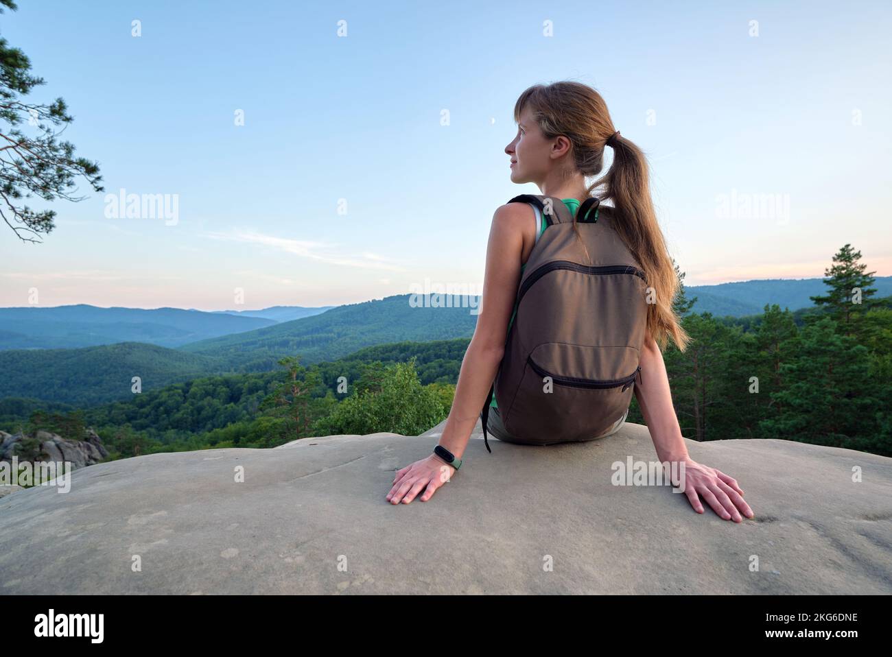 Sportive woman sitting alone taking a break on hillside trail. Female hiker enjoying view of ...