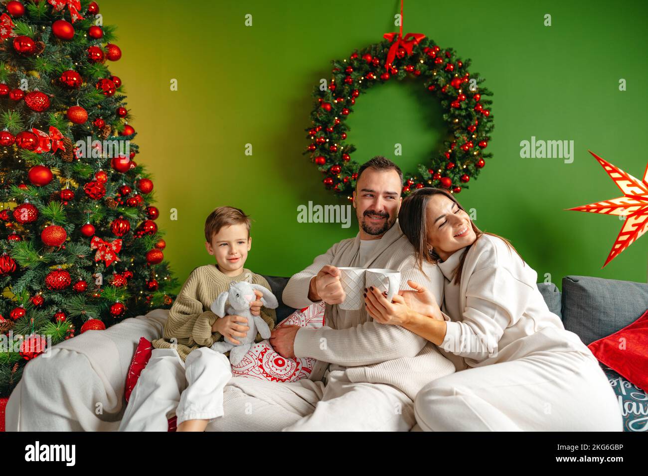 Happy young family sitting on sofa and relaxing at home at Christmas ...