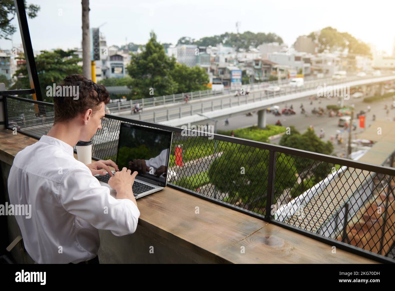 Young project manager working on laptop on rooftop of office building ...