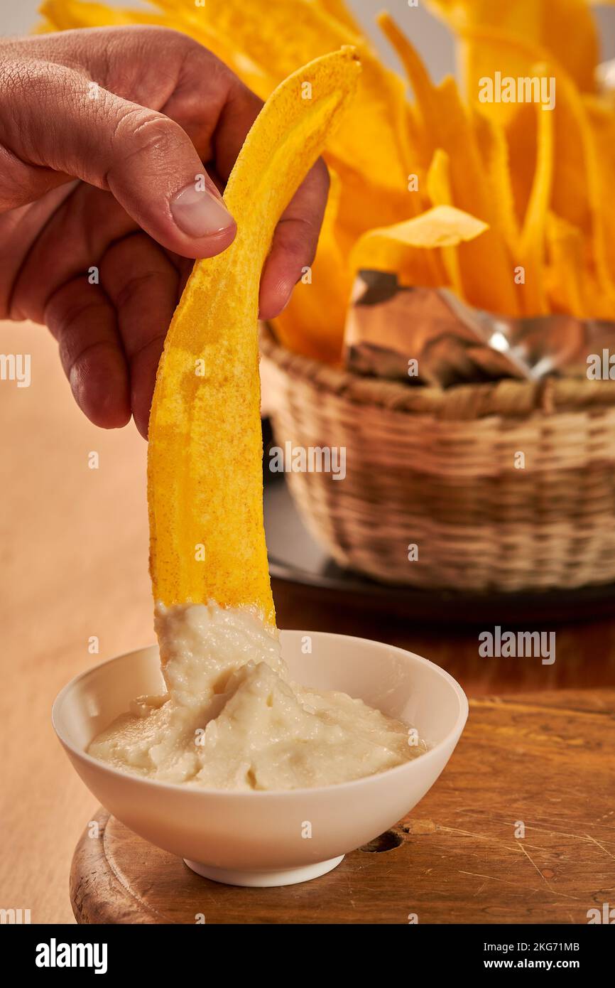 A vertical close-up of a person dipping fried mango slices in a sauce ...