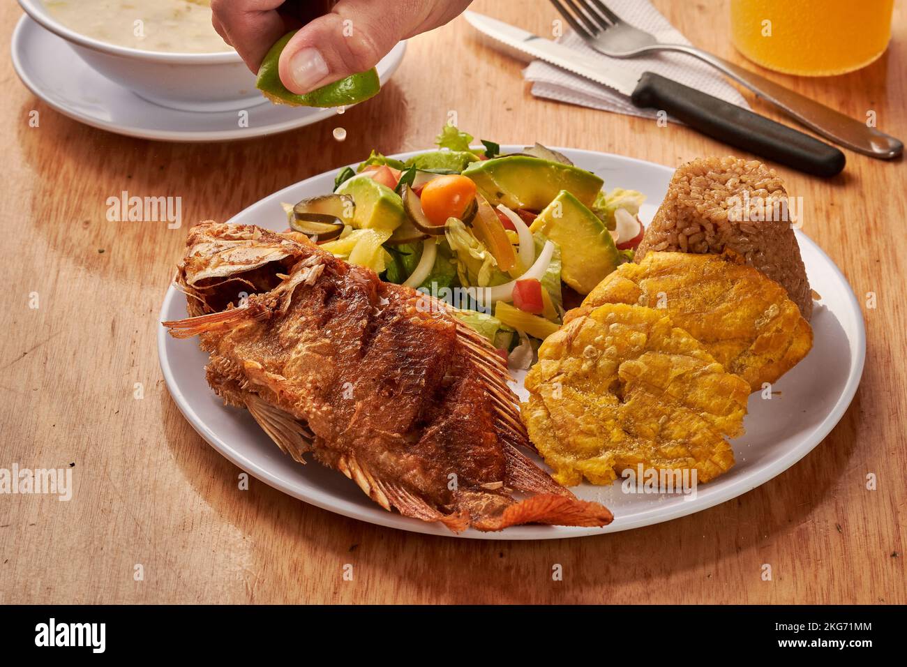 A close-up of a person squeezing lime on fried fish with salad and rice ...