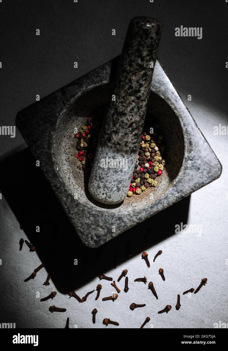 A vertical close-up shot of colorful dry peppers in a stone grinder ...