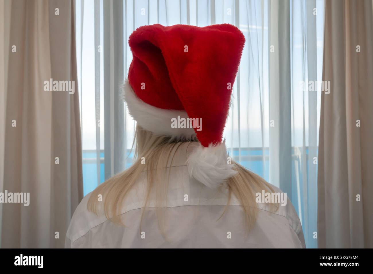 Sad young woman with drooping shoulders in a Santa Claus hat is sitting ...
