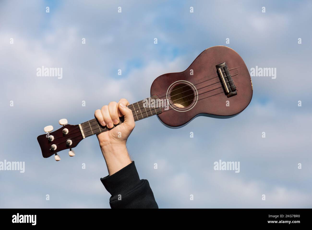 Guitar ukulele in man hand against cloudy sky, nature blurred ...
