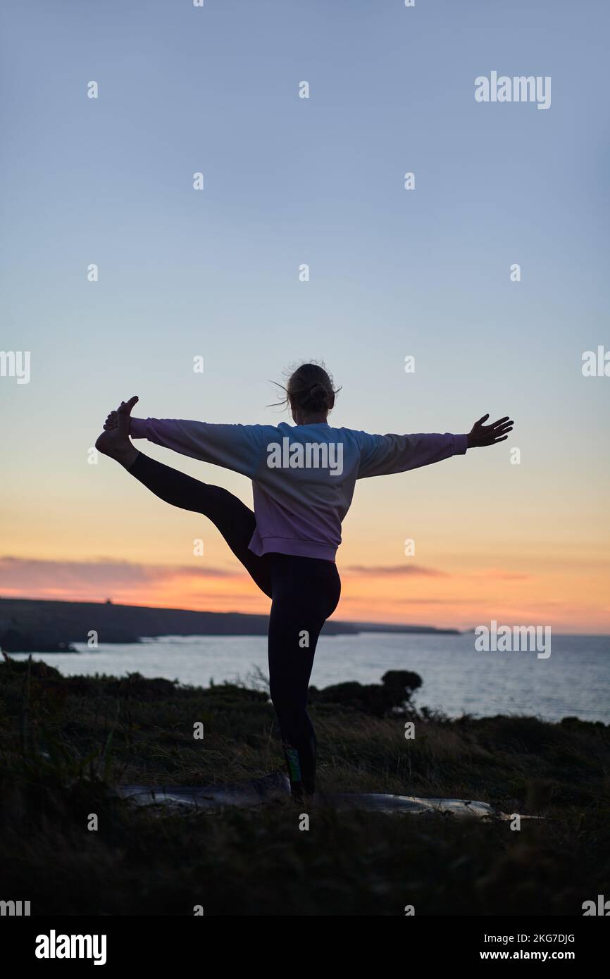 woman performing a complicated yoga position in nature at sunset with ...