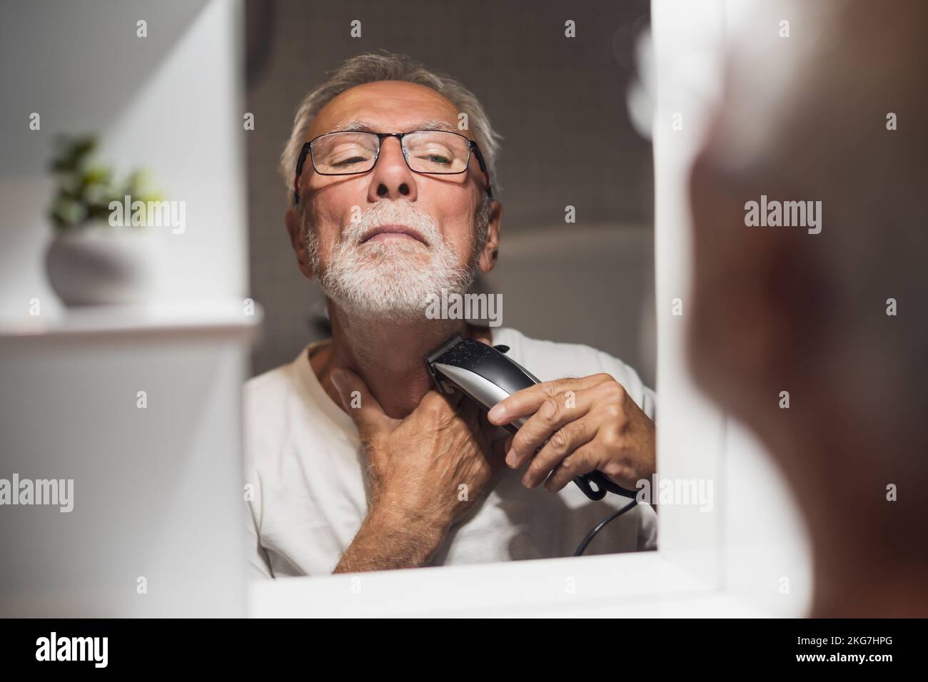 Senior man is trimming his beard with electric trimmer in bathroom ...