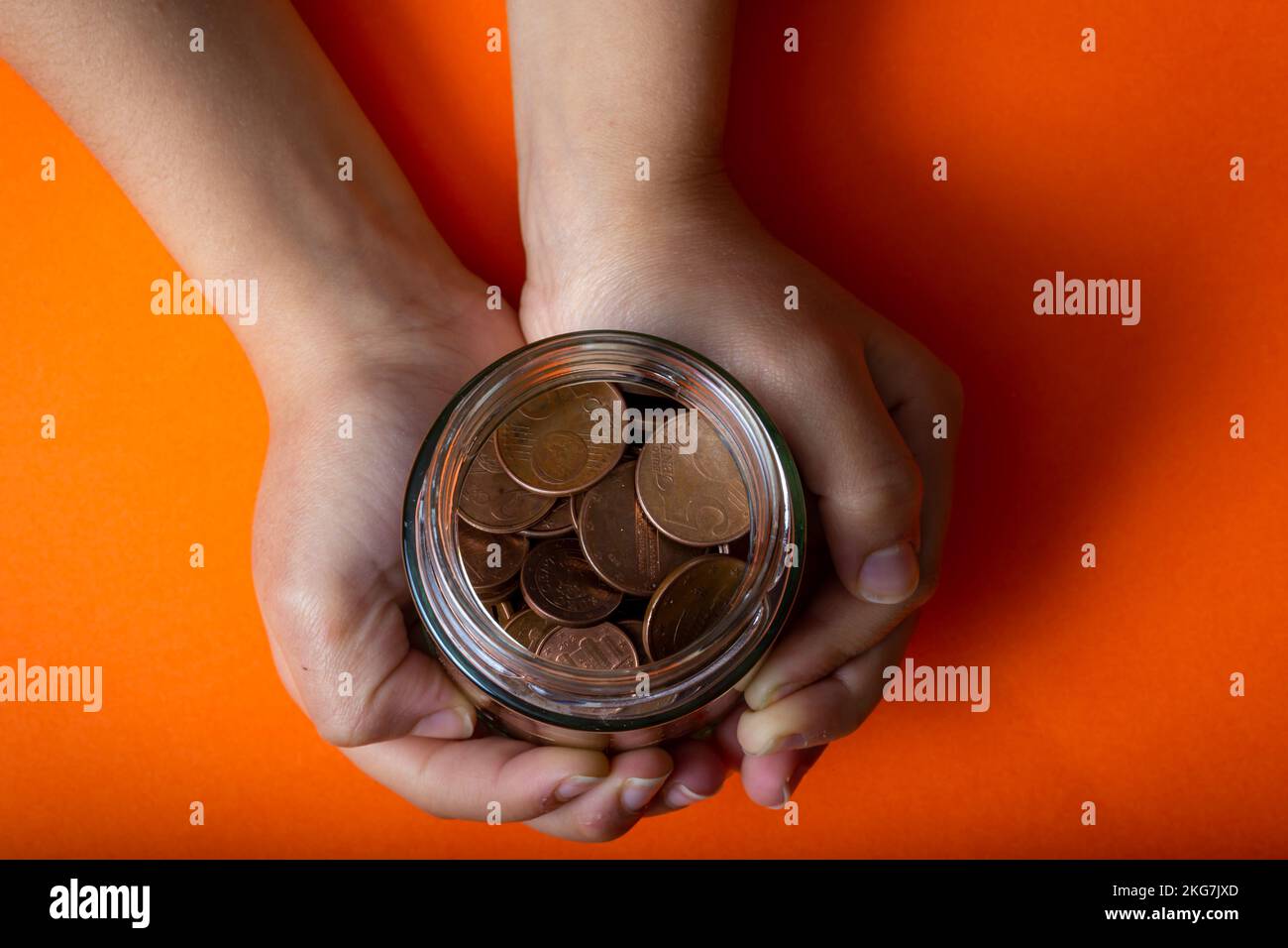 Hand holding small coins on orange background Stock Photo - Alamy