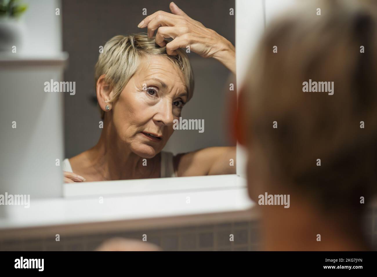 Mature woman looking at her face in the bathroom. She is examining ...
